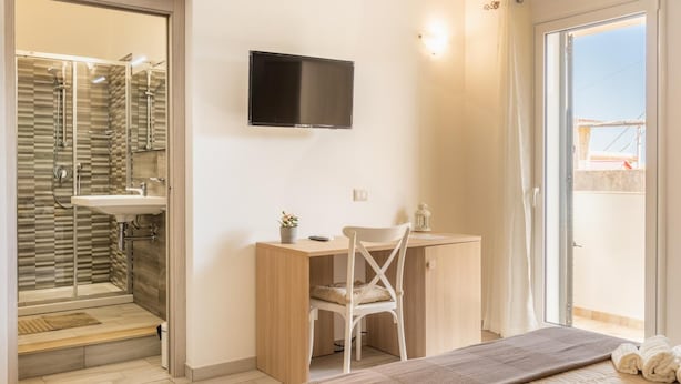 Quarto moderno com cama, escrivaninha, cadeira, televisão e área de chuveiro.