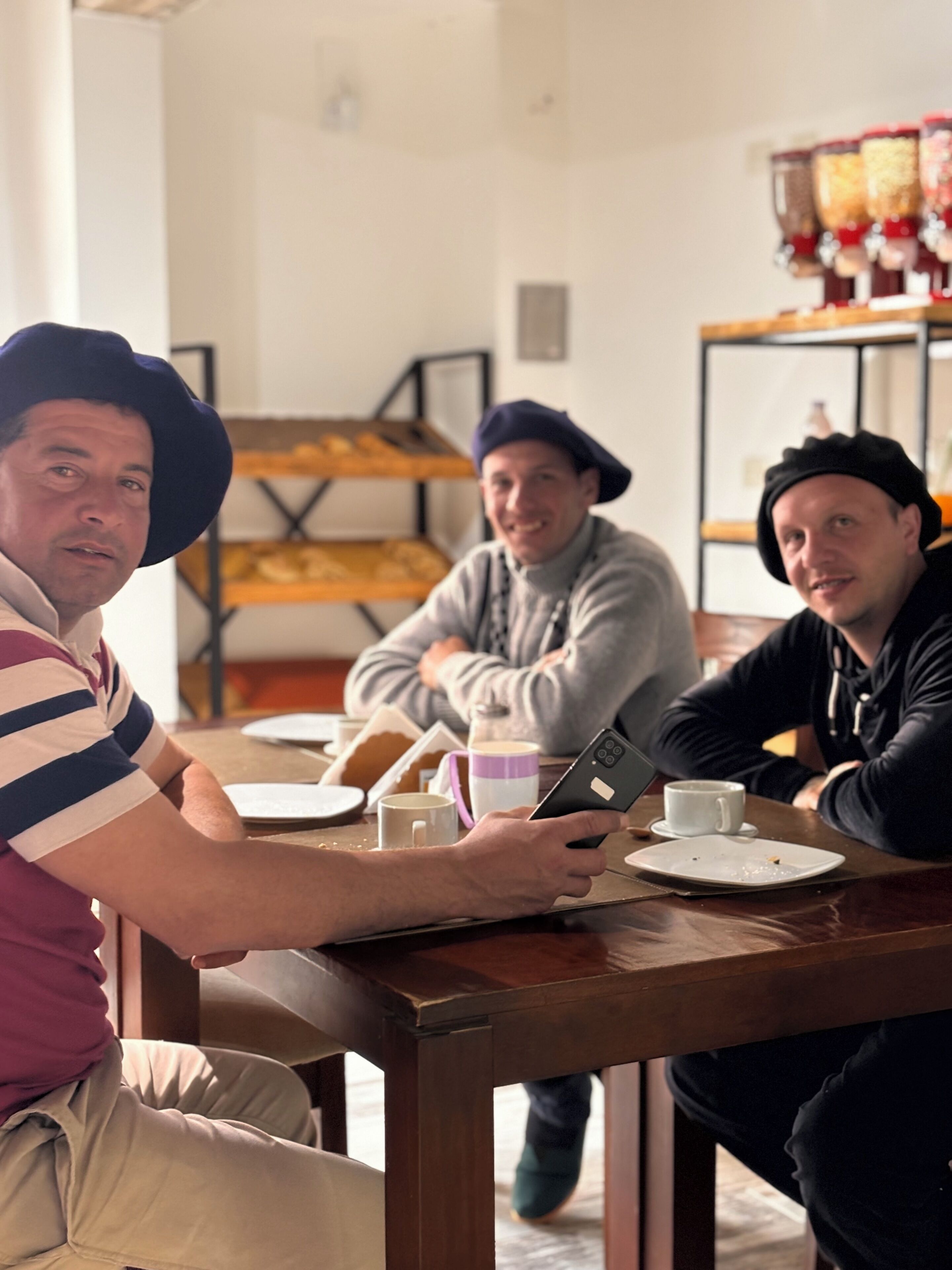 Três pessoas sentadas à mesa de madeira, com um smartphone, uma caneca e um prato.