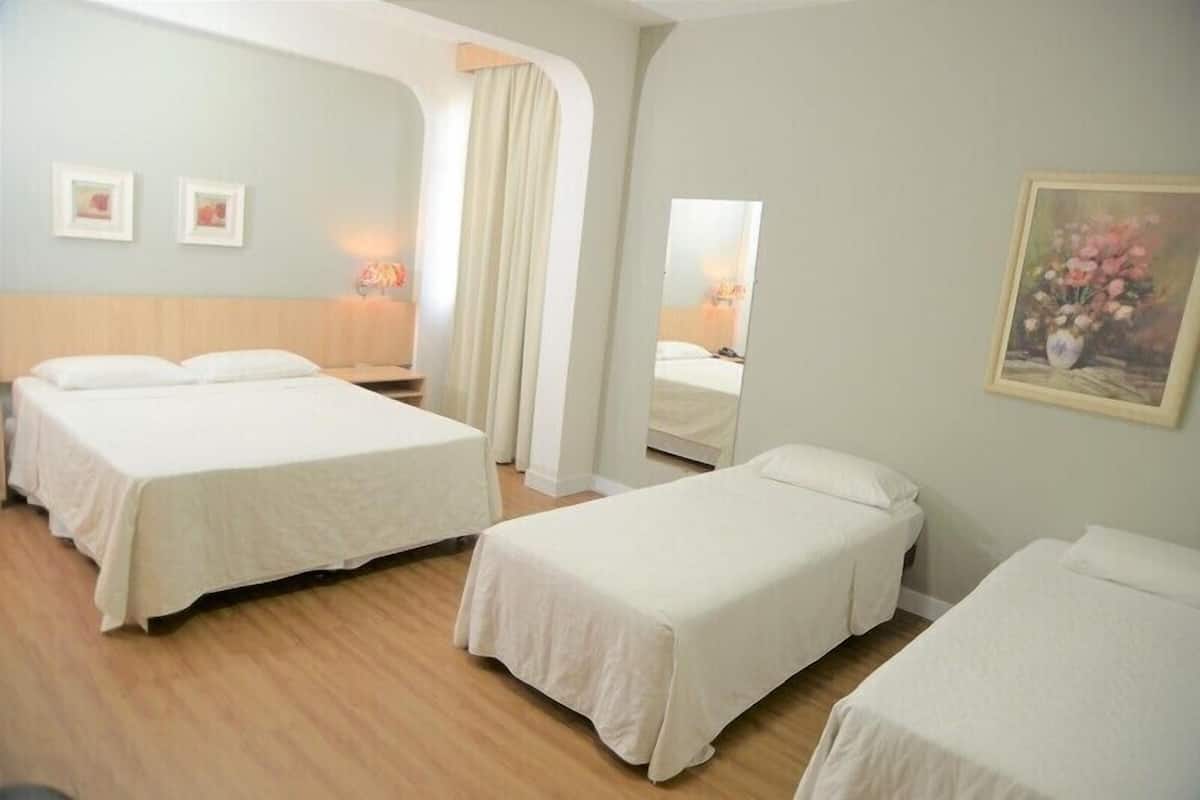 Quarto de hotel com três camas, piso de madeira e espelho na parede.
