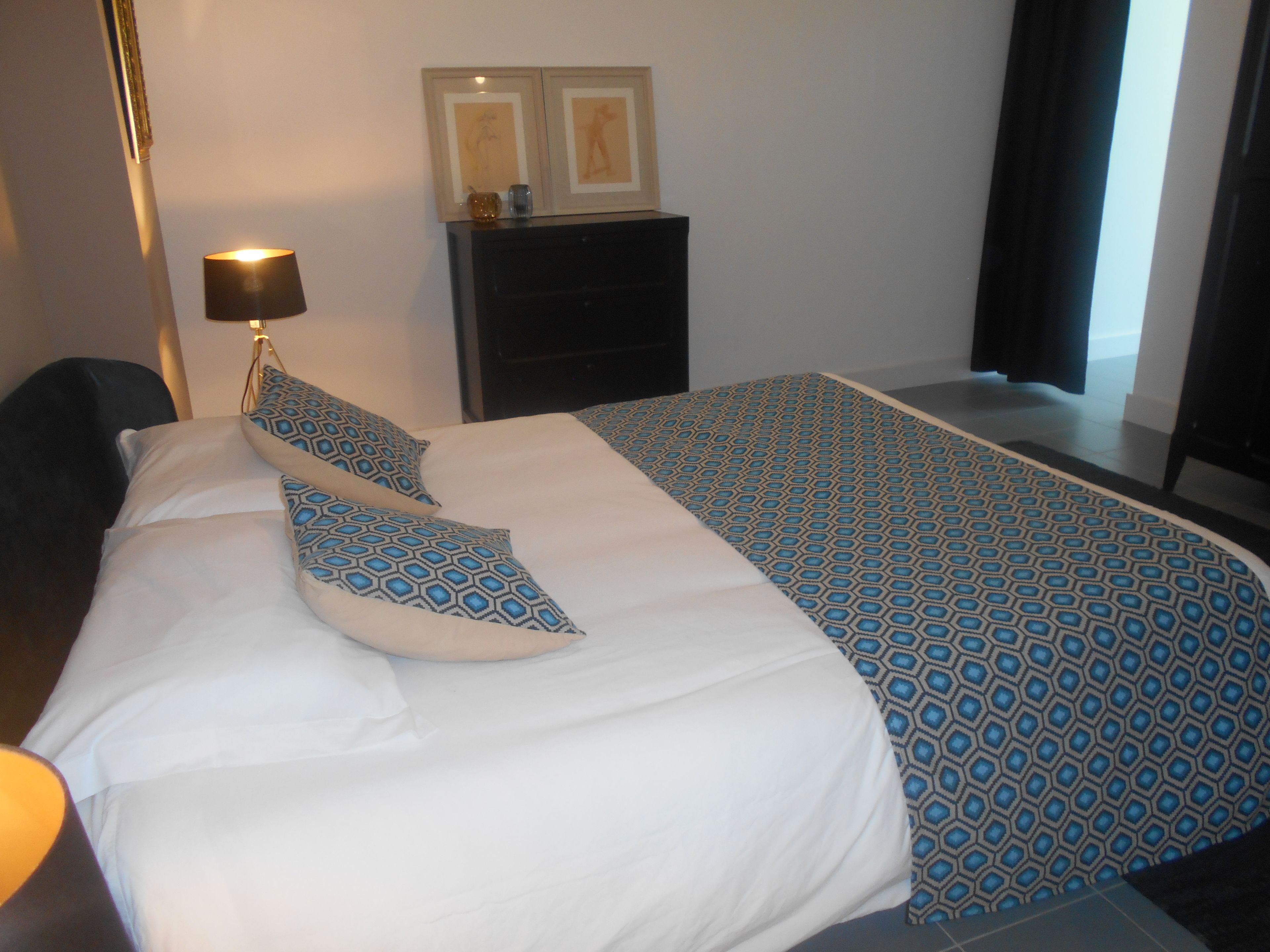 Quarto de hotel com cama, mesa de cabeceira, abajur e duas molduras na parede.