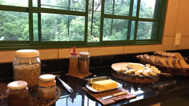 Uma bancada de cozinha com potes de geleia, um frasco de mel, uma faca e um prato de queijo e pão.