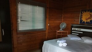 Quarto de cabana de madeira com cama, ventilador e janela com persianas.
