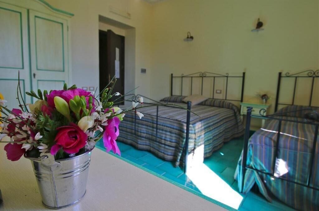 Quarto com duas camas, uma cabeceira de metal e uma pequena mesa com um vaso de flores.