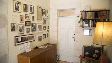 Um quarto com uma parede de fotografias emolduradas, uma escrivaninha de madeira, uma estante de livros e um abajur.