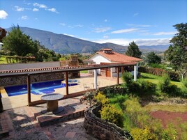 Área da piscina com um pérgola, uma parede de pedra e vista para montanhas.