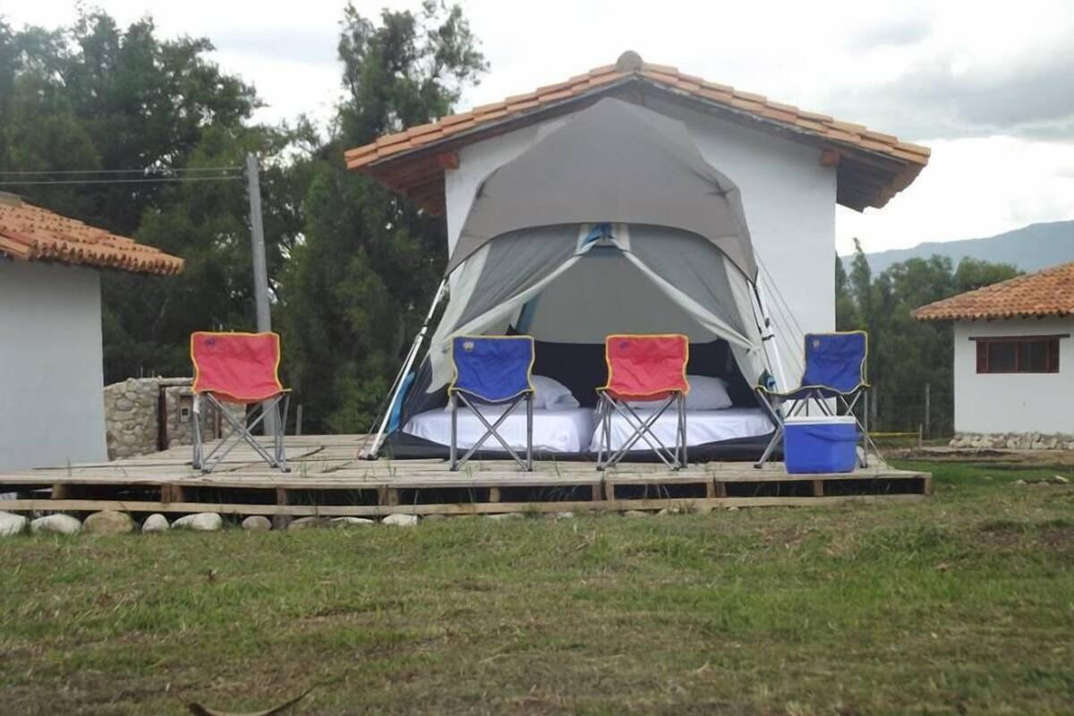 Um parque de campismo com uma tenda, quatro cadeiras dobráveis e um pequeno palco.