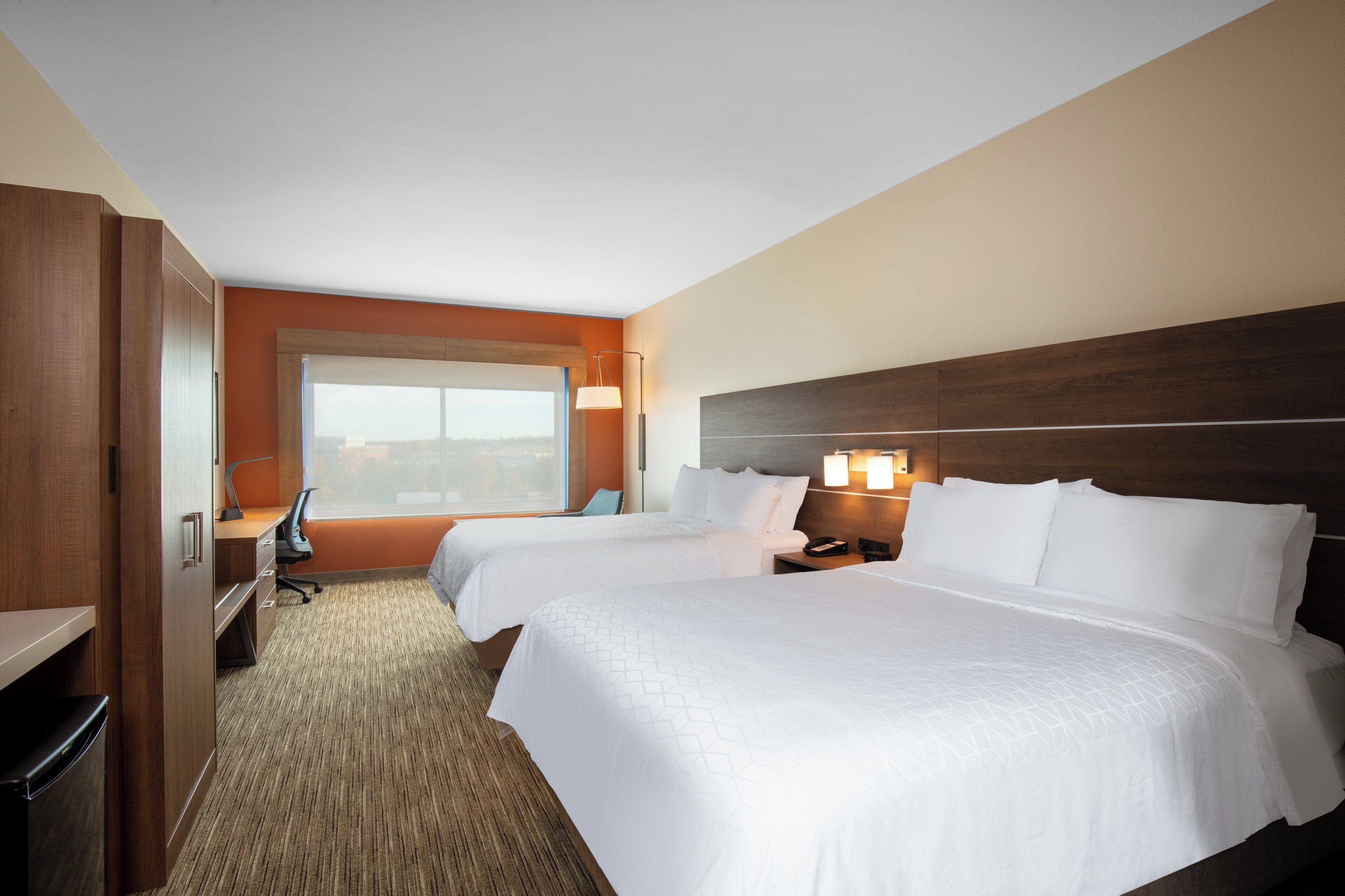 Quarto de hotel com duas camas, uma escrivaninha e uma janela grande.
