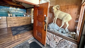 Uma área de recepção com um balcão de madeira, uma escultura de carneiro montado e um mural das montanhas do Alasca.