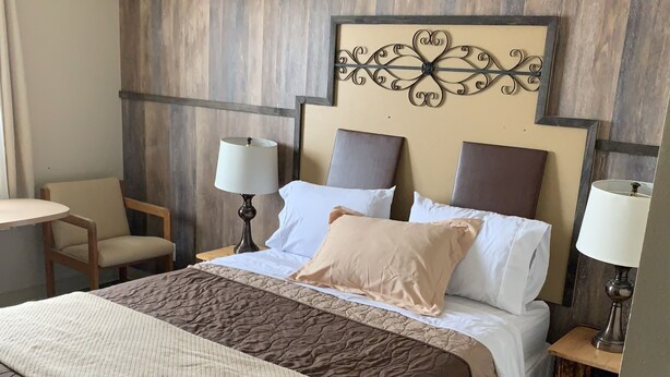 Quarto de hotel com uma cama grande, duas mesas de cabeceira com luminárias, uma cadeira e um objeto decorativo na parede.