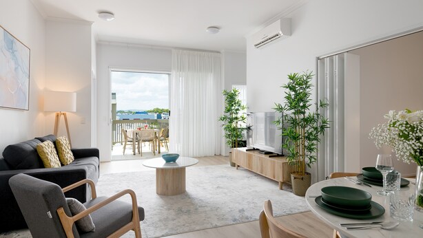 Uma sala de estar moderna com sofá, mesa de centro, mesa de jantar e televisão. Há plantas e vista para o exterior.