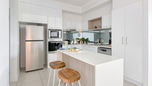 Cozinha moderna com armários brancos, geladeira de aço inoxidável, micro-ondas e uma ilha central com banquetas.