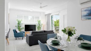 Uma sala de estar moderna com sofá, televisão e área de jantar com mesa posta para dois.