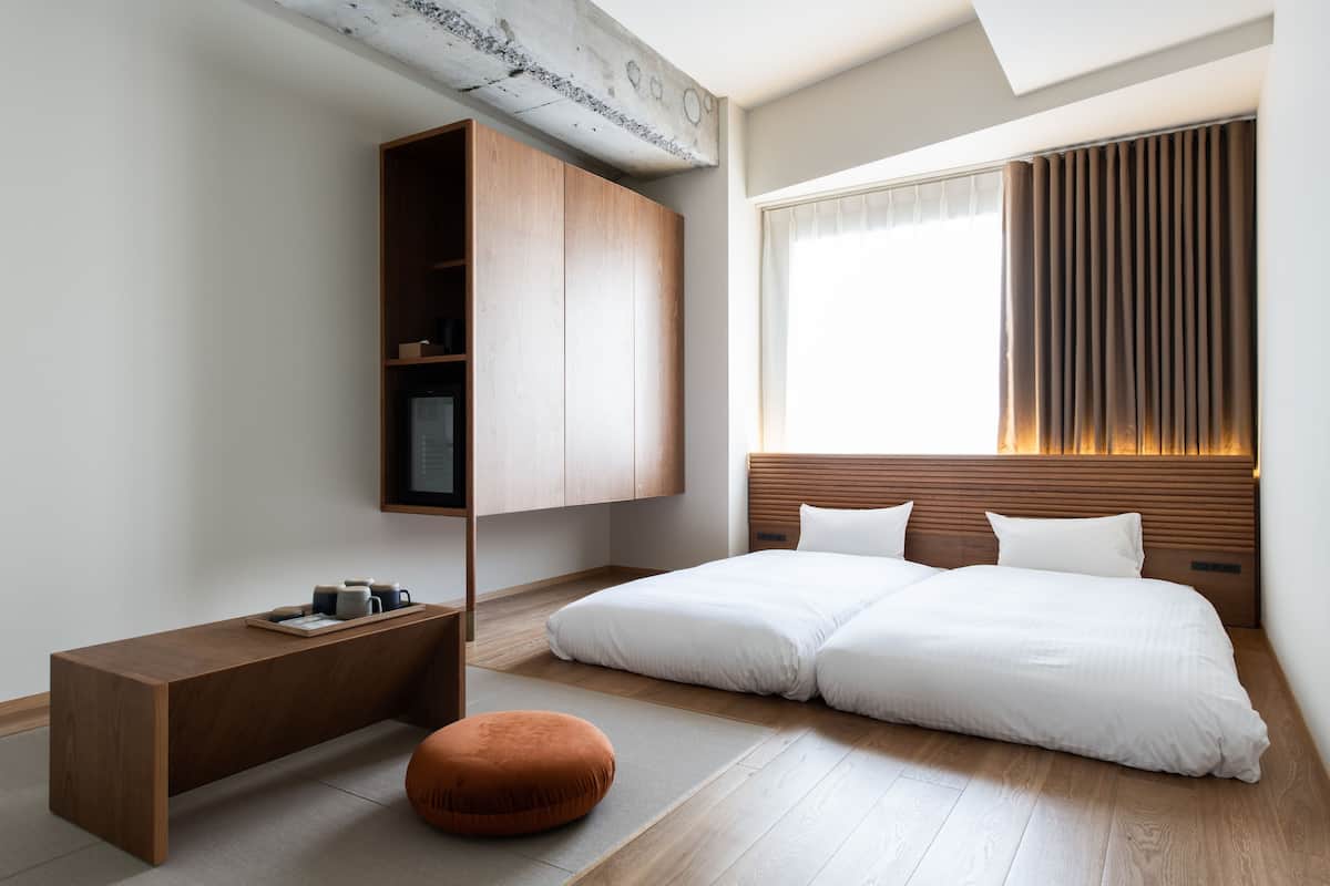 Quarto moderno com cama, um banquinho de madeira, um pequeno apoio para os pés e uma prateleira embutida para televisão.
