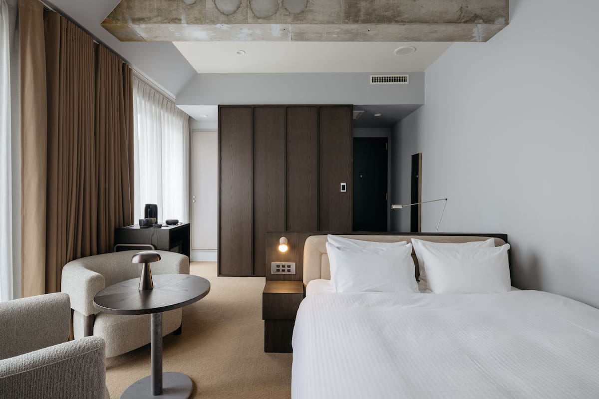 Quarto de hotel moderno com uma cama grande, uma mesa redonda, um sofá e uma escrivaninha com abajur.