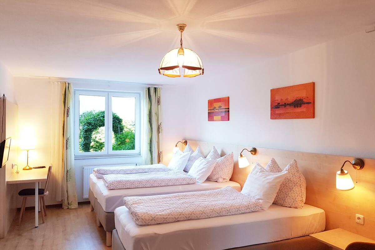 Quarto de hotel com duas camas, uma escrivaninha e uma janela com cortinas.