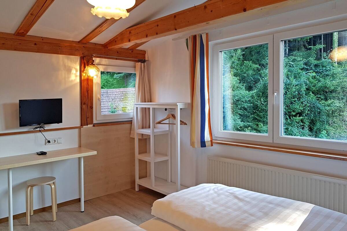 Quarto com cama, escrivaninha com cadeira, televisão e janela com cortinas.