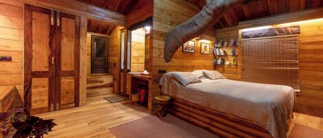 Quarto de cabana de tronco com uma cama, paredes de madeira, uma pedra grande e uma estante.
