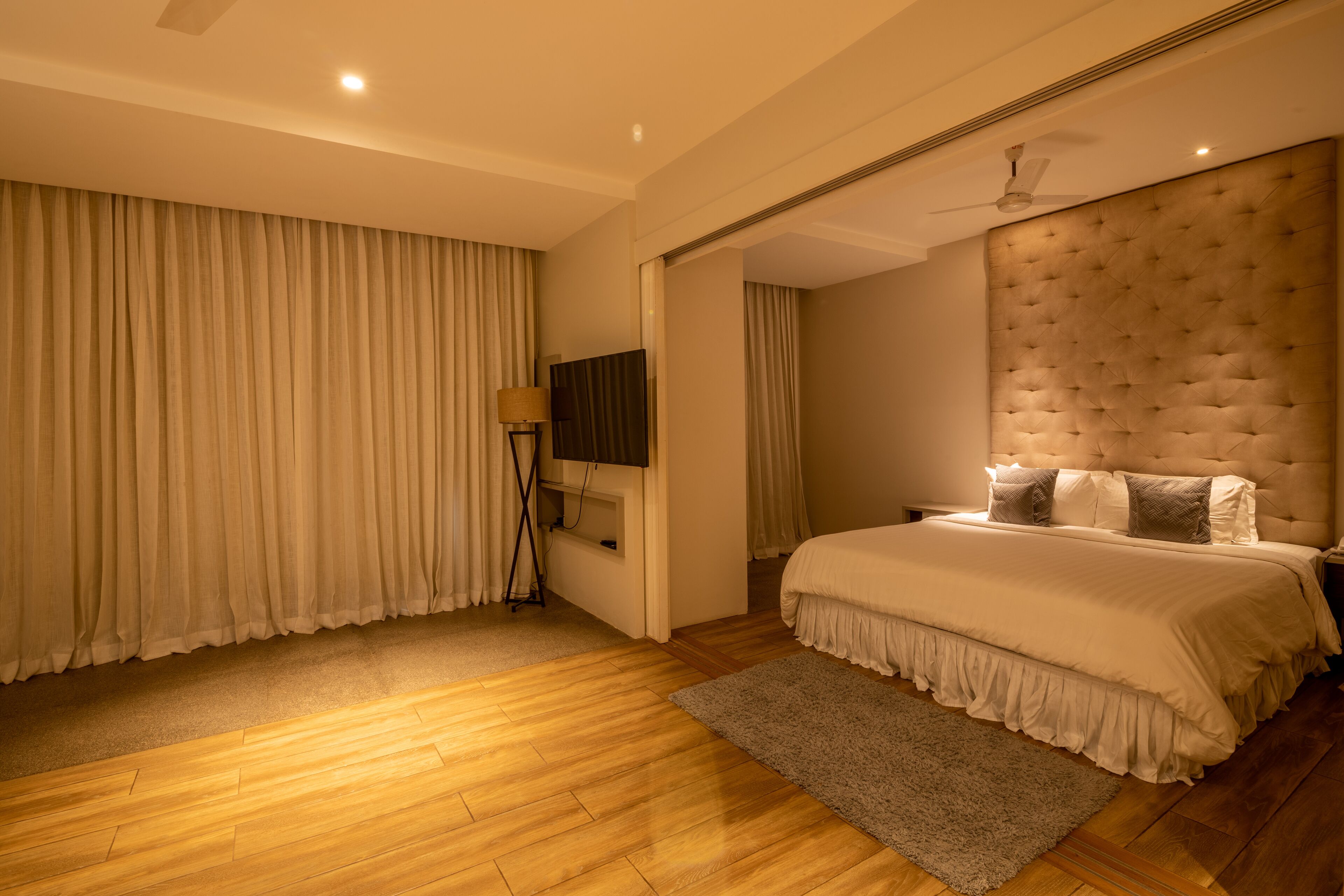 Quarto com uma cama grande, um ventilador de teto e uma TV na parede.