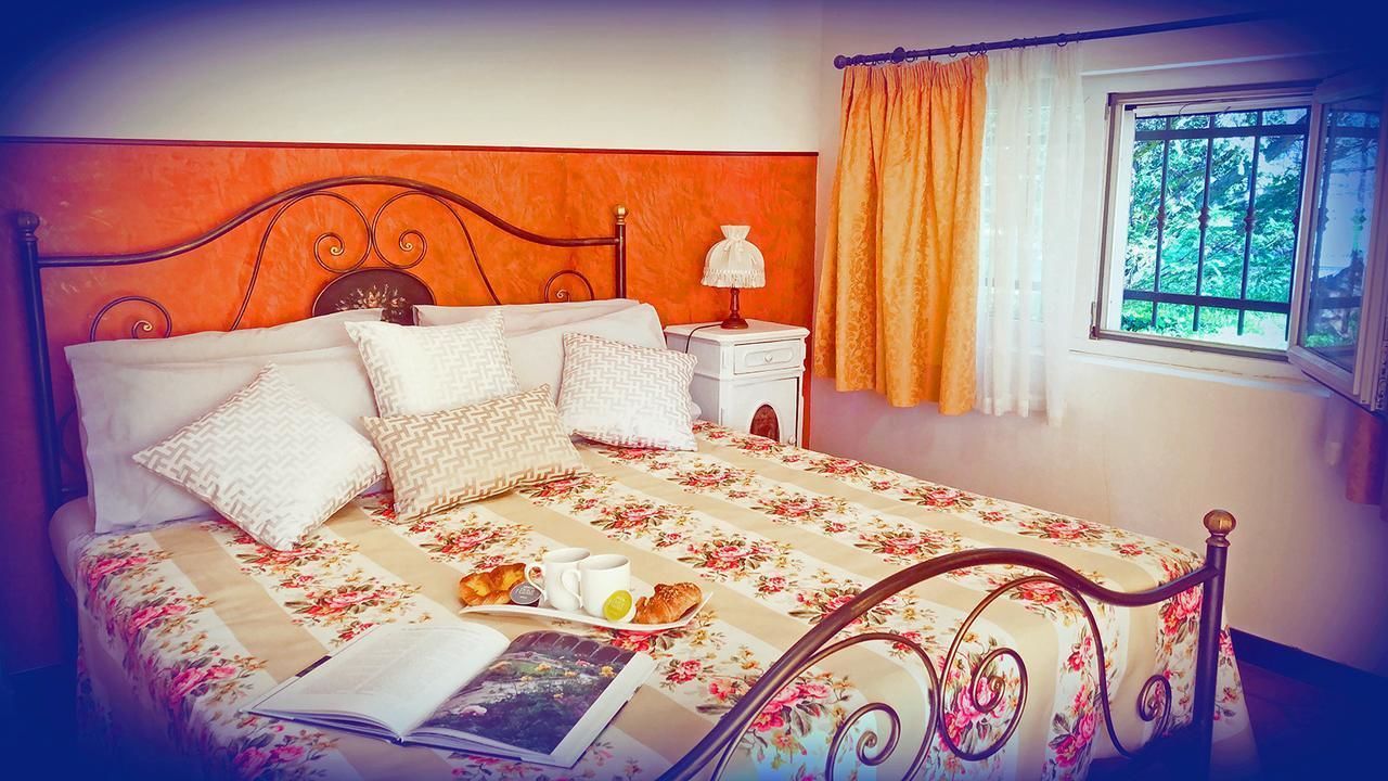 Cama bem arrumada com colcha florida, mesa de cabeceira com abajur e janela com cortinas.