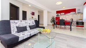Uma sala de estar moderna com um sofá, uma mesa de centro de vidro e uma área de cozinha com armários vermelhos e uma mesa de jantar.