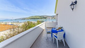 Varanda com mesa e cadeiras, vista para a costa com edifícios e vegetação.