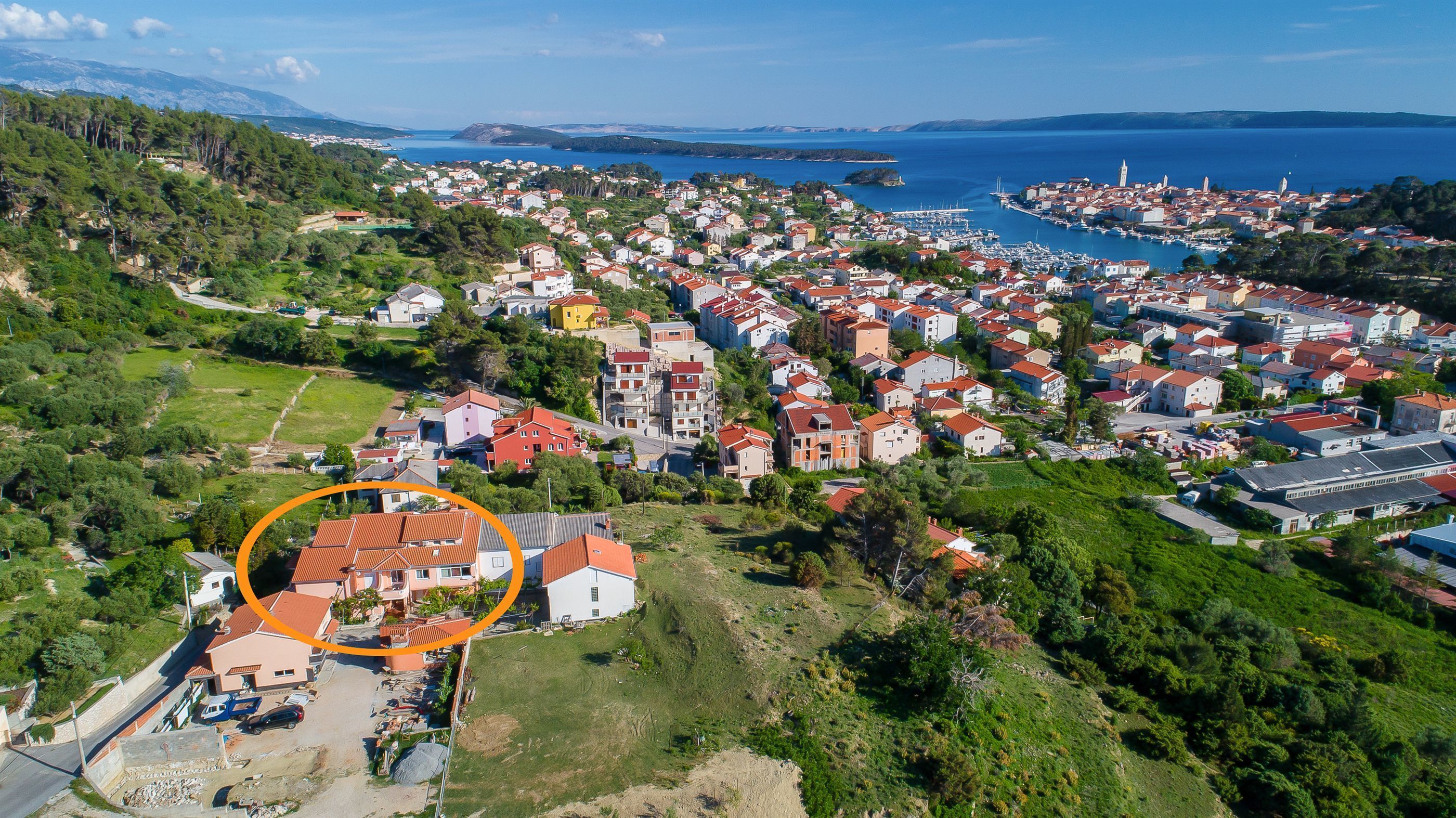 Vista aérea de uma cidade costeira com habitação densa, um porto de iates e uma torre de igreja imponente.