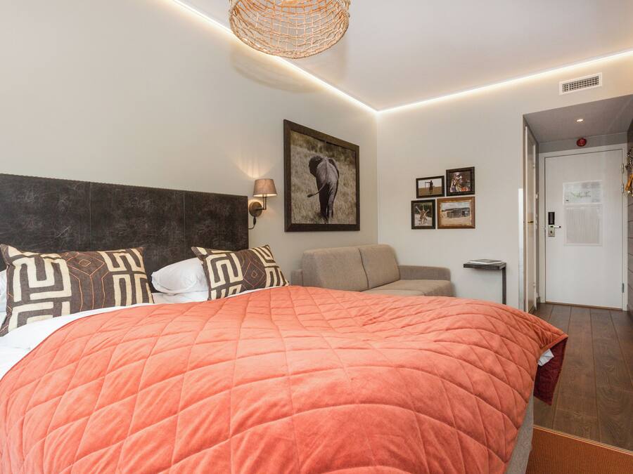 Quarto de hotel com uma cama grande, cabeceira, luminária fixada na parede e um quadro emoldurado.