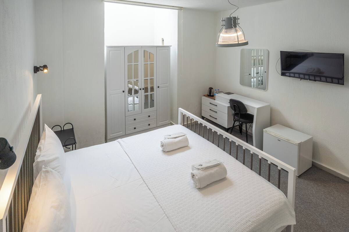Um quarto com cama, escrivaninha, cadeira, televisão e guarda-roupa.