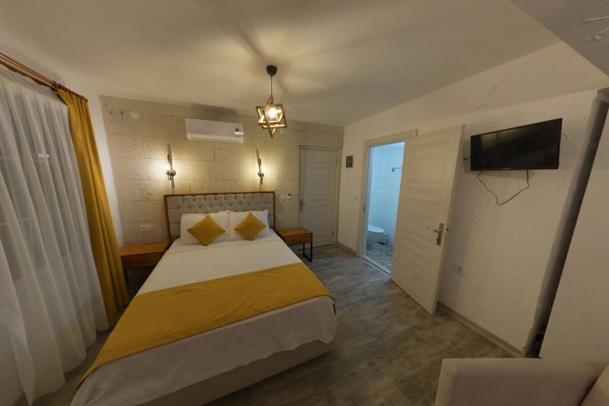Quarto de hotel com cama, televisão, ar condicionado e porta que dá para outro cômodo.