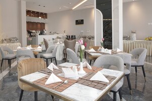Um restaurante moderno com mesas de bancada em mármore, cadeiras estofadas em cinza e uma área de cozinha central.
