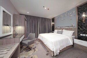 Quarto de hotel moderno com uma cama grande, uma mesa com cadeira, um espelho e uma parede decorativa com um mural floral.