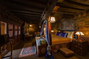 Quarto tradicional com cama de dossel, escrivaninha de madeira e tapete estampado.