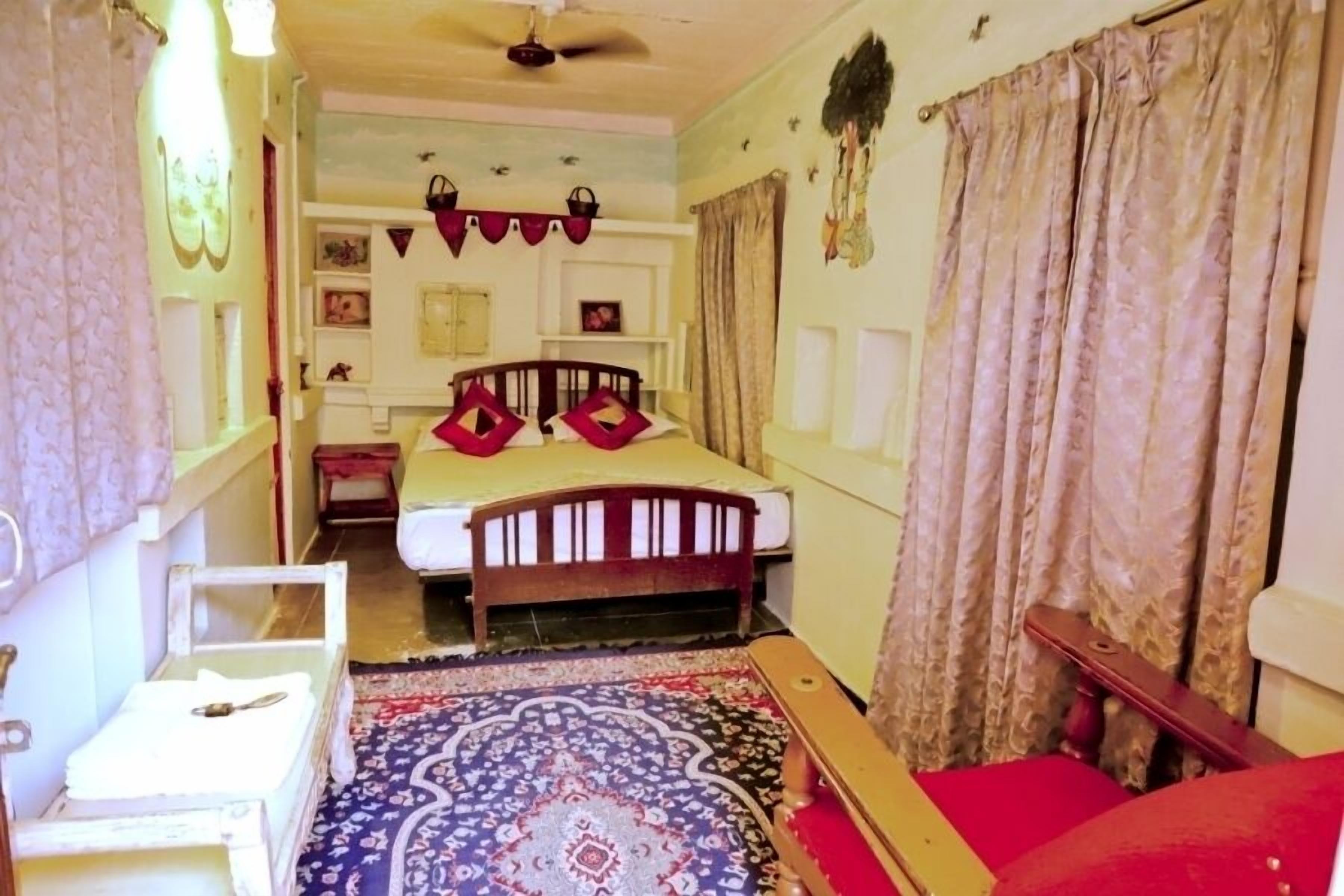 Quarto com cama, uma mesinha, cadeira e tapete estampado.