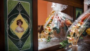 Um retrato emoldurado com moldura decorativa, um espelho com arranjos florais e um pequeno vaso com flores.