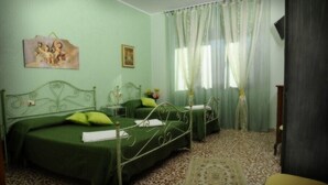 Quarto com duas camas, roupa de cama verde, tapete estampado e uma janela com cortinas leves.