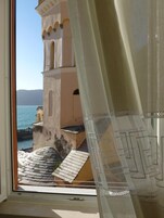 Vista da janela de um edifício costeiro, com uma escadaria de pedra a levar a uma varanda, com vista para o mar.