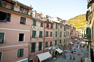 Uma rua estreita com edifícios altos, varandas e uma colina ao fundo.