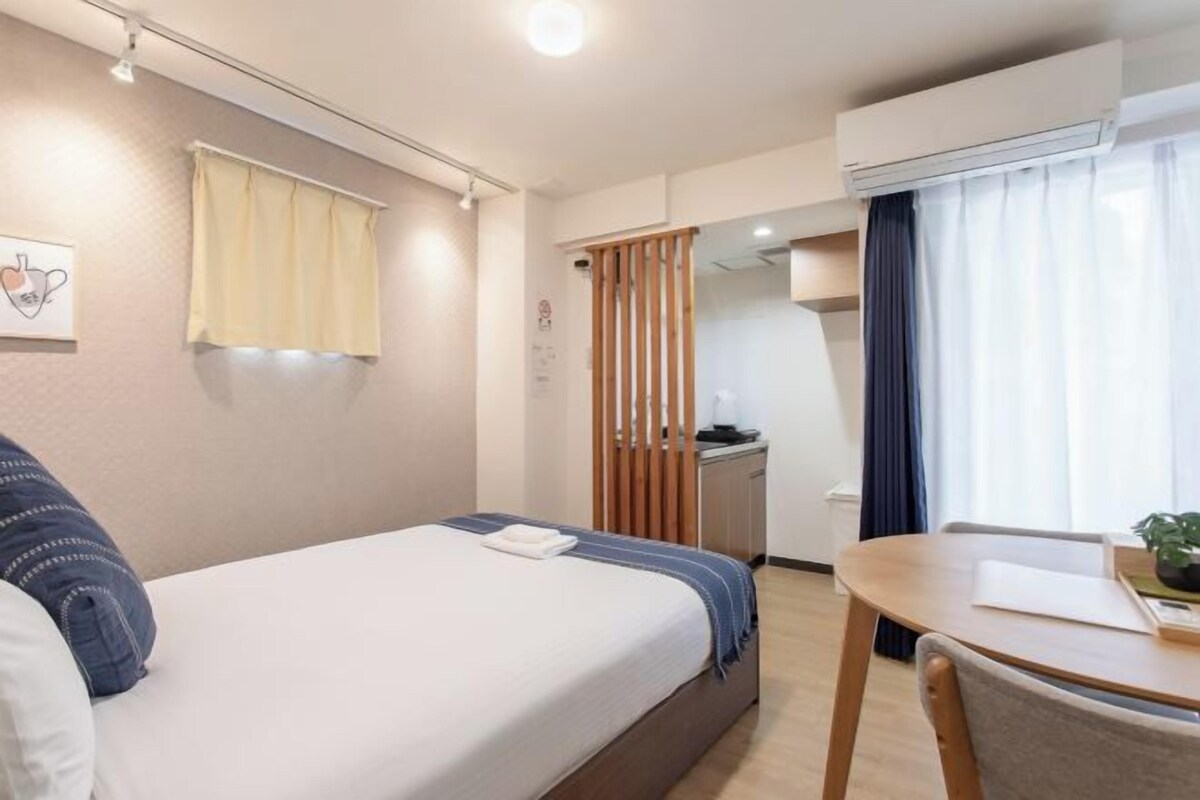 Quarto de hotel com cama, escrivaninha, cadeira e janela com cortinas.
