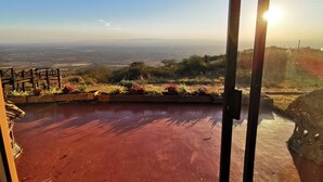 Vista de uma varanda com piso vermelho, guarda-corpo de madeira e plantas em vasos.