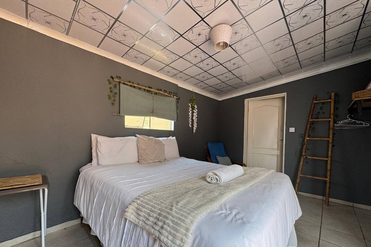 Um quarto com uma cama, uma mesa pequena, uma cadeira, uma escada e uma porta.