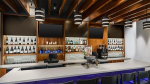 Uma área de bar com um balcão comprido, várias prateleiras de garrafas e banquetas.