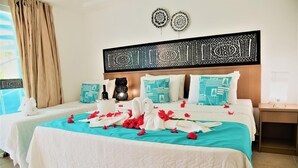 Quarto de hotel com uma cama grande, duas mesas de cabeceira, um painel de cabeceira decorativo e vista para o mar.