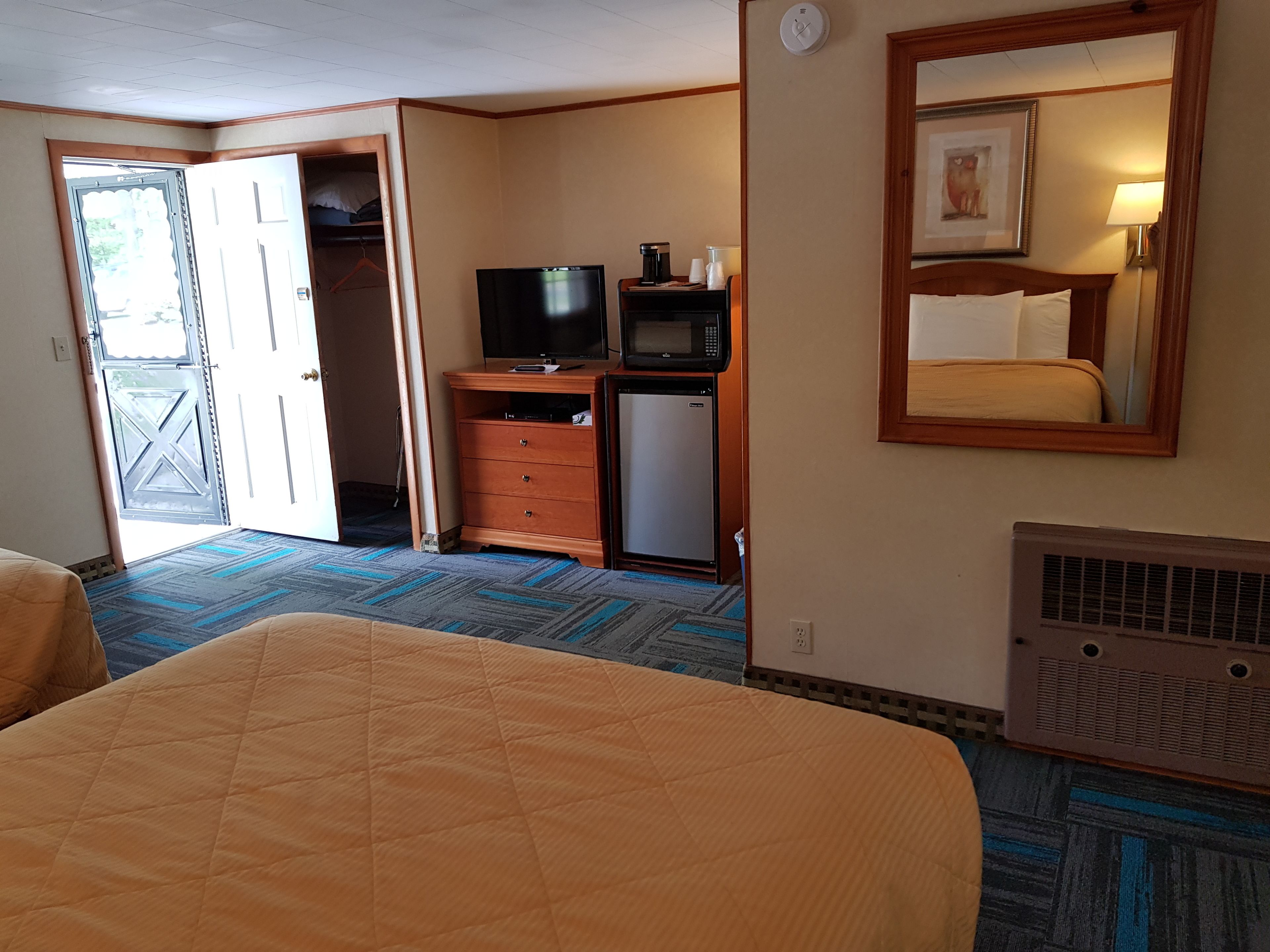 Quarto de hotel com cama, escrivaninha, televisão, micro-ondas e um pequeno frigorífico.