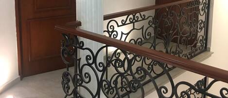 Uma porta de madeira, um pilar branco e um corrimão de metal com detalhes elaborados.