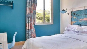 Um quarto com cama, janela com cortinas e luminária fixada na parede.