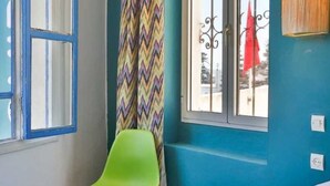 Quarto com janela, uma cadeira e cortina estampada.