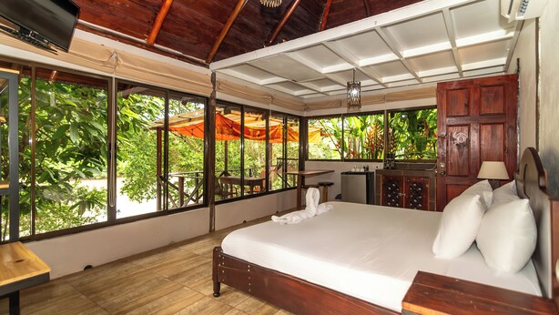 Quarto espaçoso com uma cama grande, mobiliário de madeira e janelas amplas com vista para o verde.