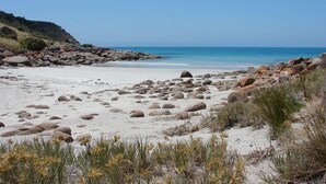 Uma praia com grandes rochas e vegetação escassa.