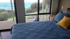 Quarto com uma cama grande, vista para o oceano e um deck de madeira.