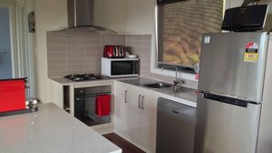 Cozinha compacta com fogão a gás, micro-ondas, geladeira de aço inoxidável e janela com vista para árvores.